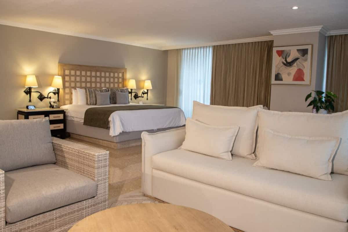 Quarto de hotel com uma cama, duas mesas de cabeceira com luminárias, um sofá e uma pequena mesa redonda.