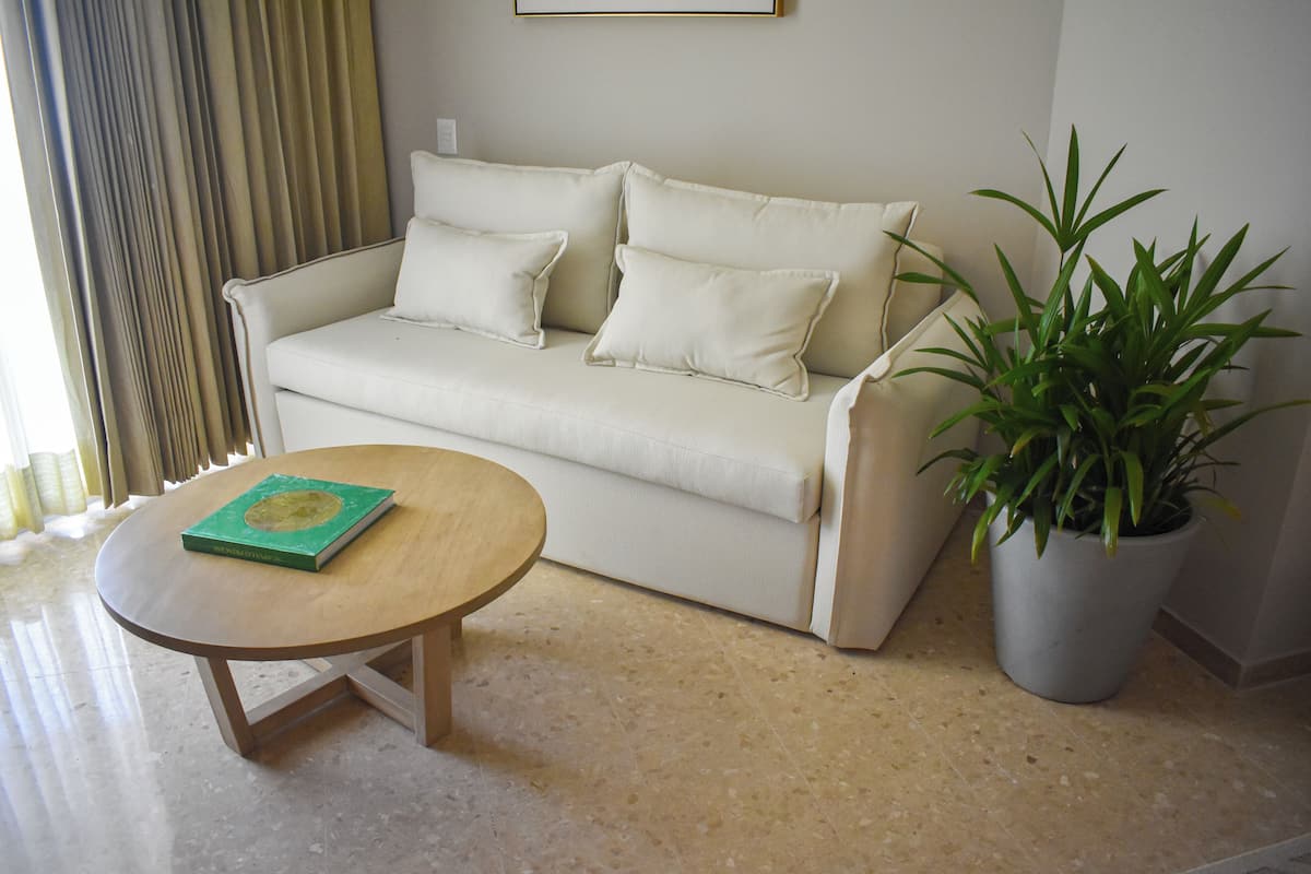 Uma sala de estar com um sofá bege, uma mesa de centro redonda de madeira e um vaso com planta.