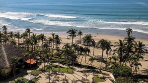 Uma praia com palmeiras, um edifício com telhado de palha e vista para o oceano.
