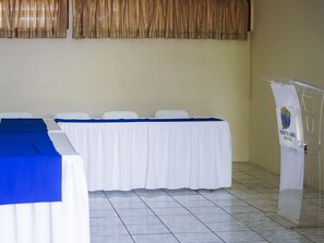 Sala de conferências com mesa branca, toalha de mesa azul e cadeiras brancas.