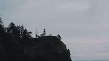 Uma paisagem costeira com um farol em um penhasco, costa rochosa e mar calmo.