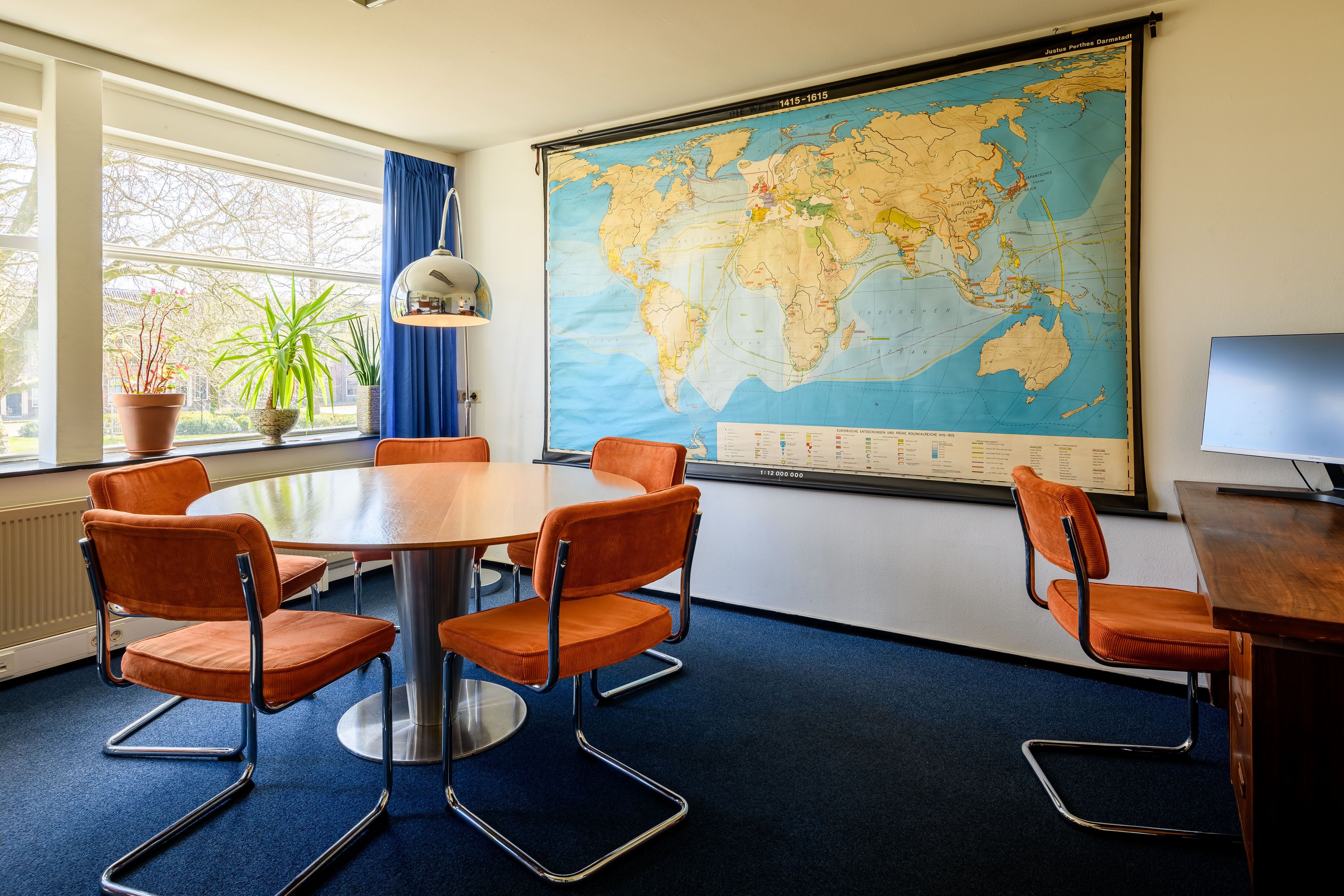 Uma sala de conferências com um grande mapa-múndi, uma mesa redonda e cadeiras laranja.