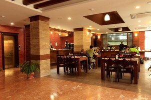 Restaurante com mesas e cadeiras de madeira, área de bar e elevador visível.
