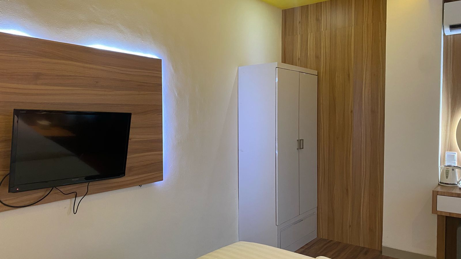 Quarto com televisão na parede, guarda-roupa branco e armário de madeira.