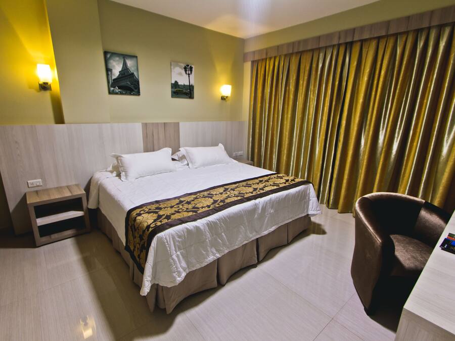 Quarto de hotel com uma cama grande, mesa de cabeceira, cadeira e escrivaninha.