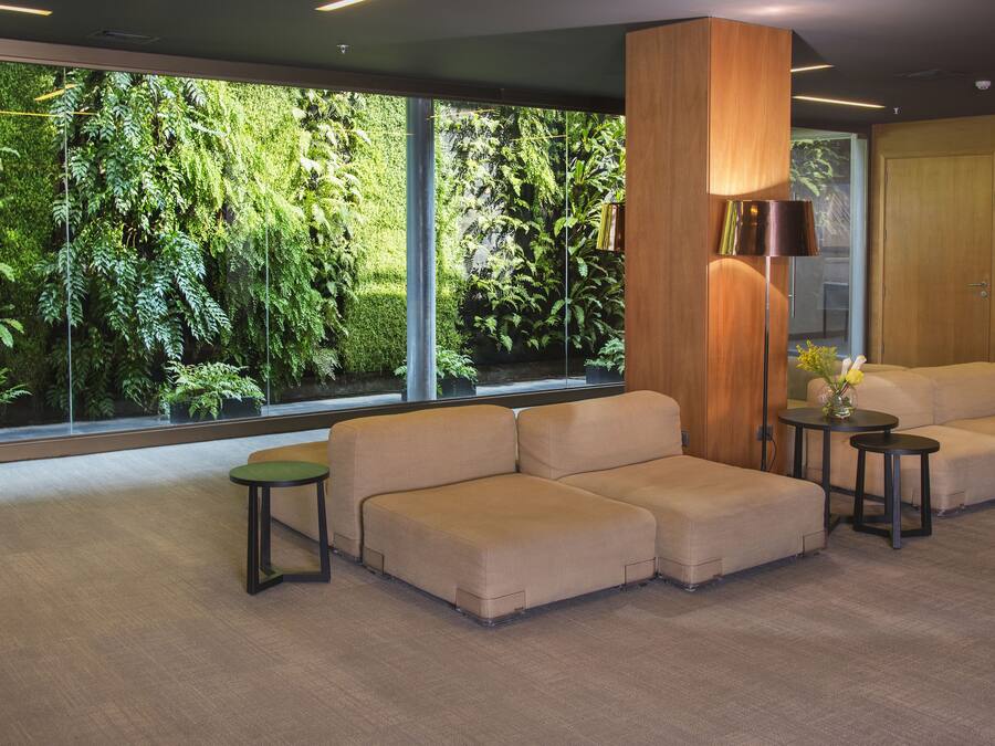 Uma área de espera moderna com uma janela grande, um sofá, uma mesa pequena e um abajur.