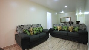 Sala de estar com dois sofás cinza escuro com estampas florais e almofadas verdes e douradas, um espelho grande na parede e piso de madeira.