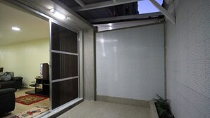 Quarto com porta de vidro deslizante para uma varanda, uma pequena área de estar com sofá e televisão, e parede revestida de azulejos.