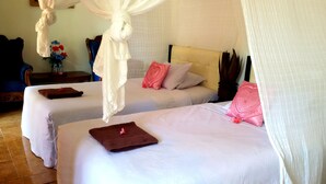 Quarto de hotel com duas camas, cada uma com dossel, roupa de cama branca e almofadas cor de rosa.