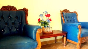 Duas poltronas azuis estofadas com braços de madeira e uma pequena mesa de madeira com um vaso de flores.