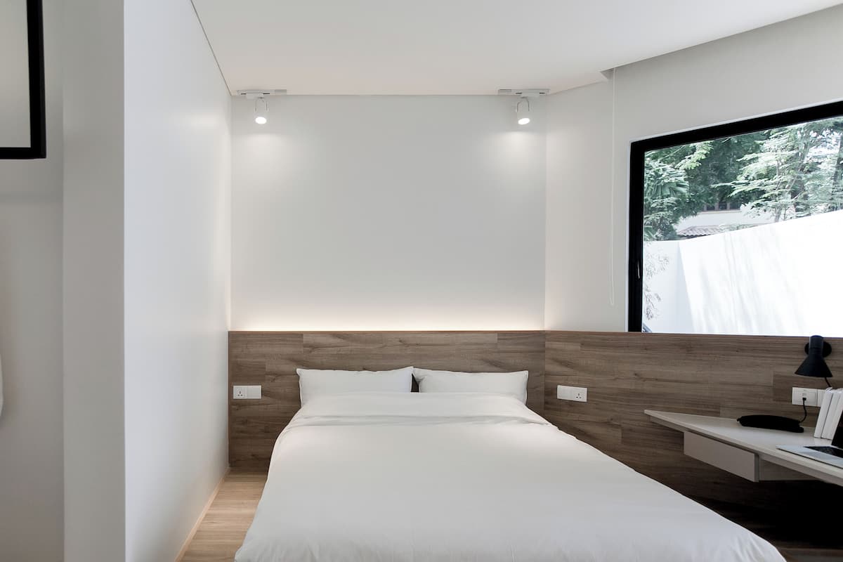 Quarto moderno com cabeceira de madeira, uma janela grande e mesa de cabeceira com abajur.