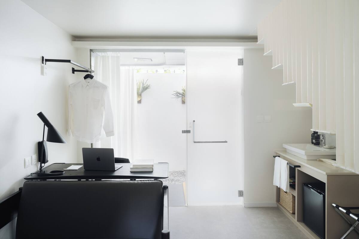 Quarto moderno e minimalista com escrivaninha, cadeira, laptop e uma pequena cozinha compacta.