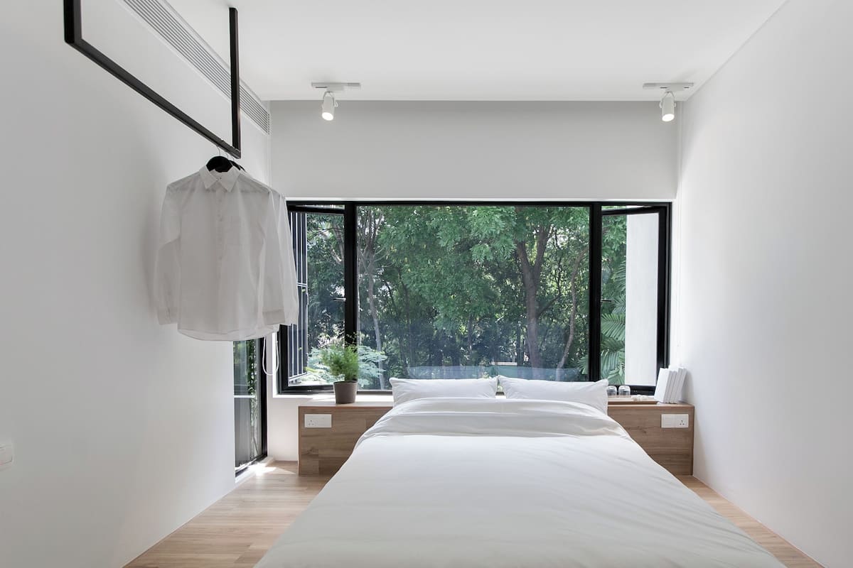 Um quarto moderno com uma cama grande, uma janela com vista para árvores e uma mesa de cabeceira com abajur.