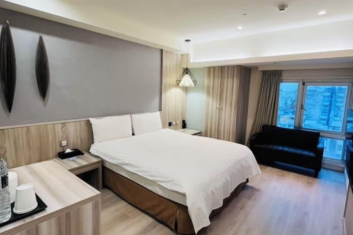 Quarto de hotel moderno com uma cama grande, mesas de cabeceira, um piano e vista para o exterior.