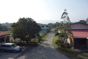 Rua residencial com casas, um carro estacionado e um acesso com árvores.