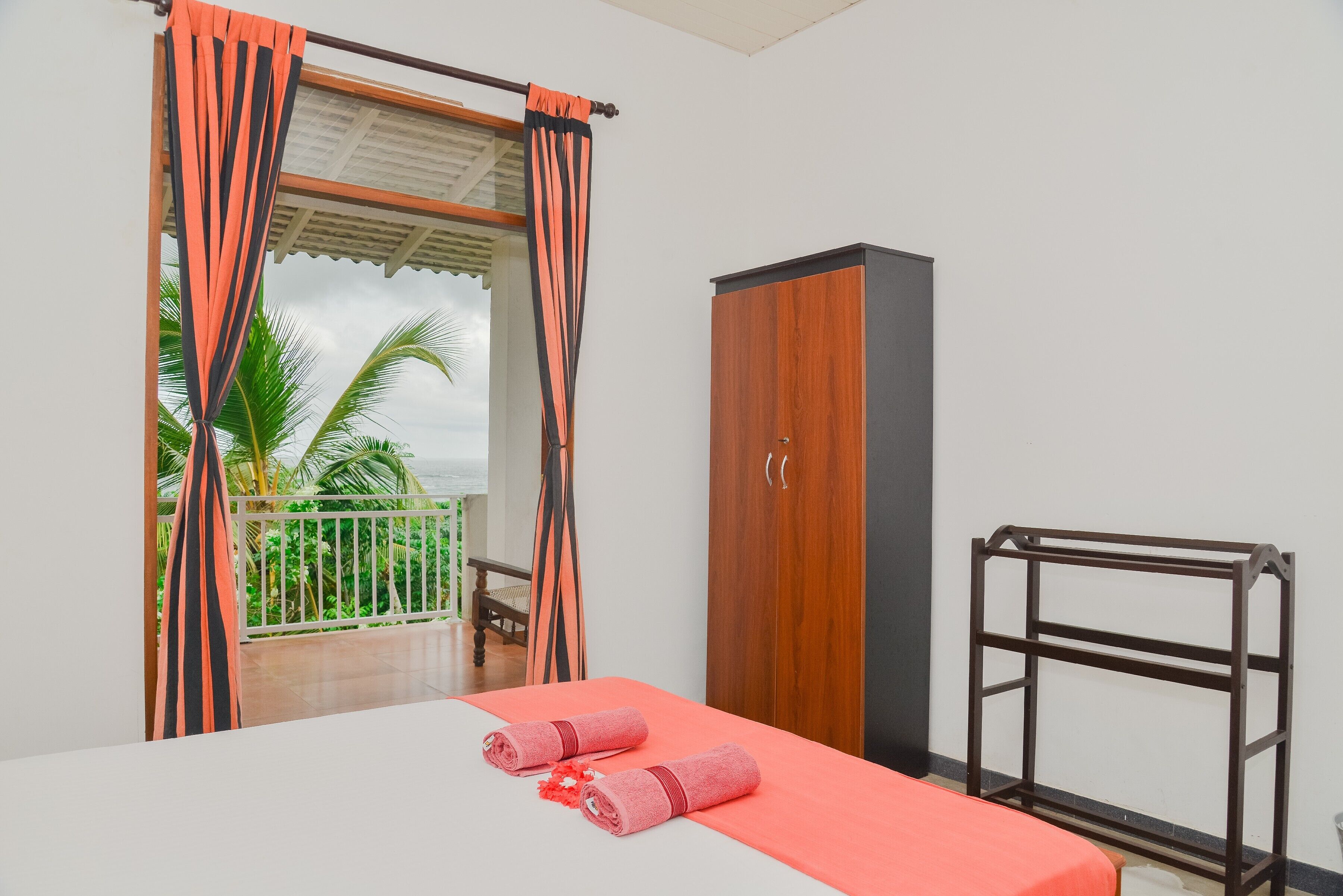 Quarto com cama, armário de madeira, suporte de metal e varanda com cortinas.