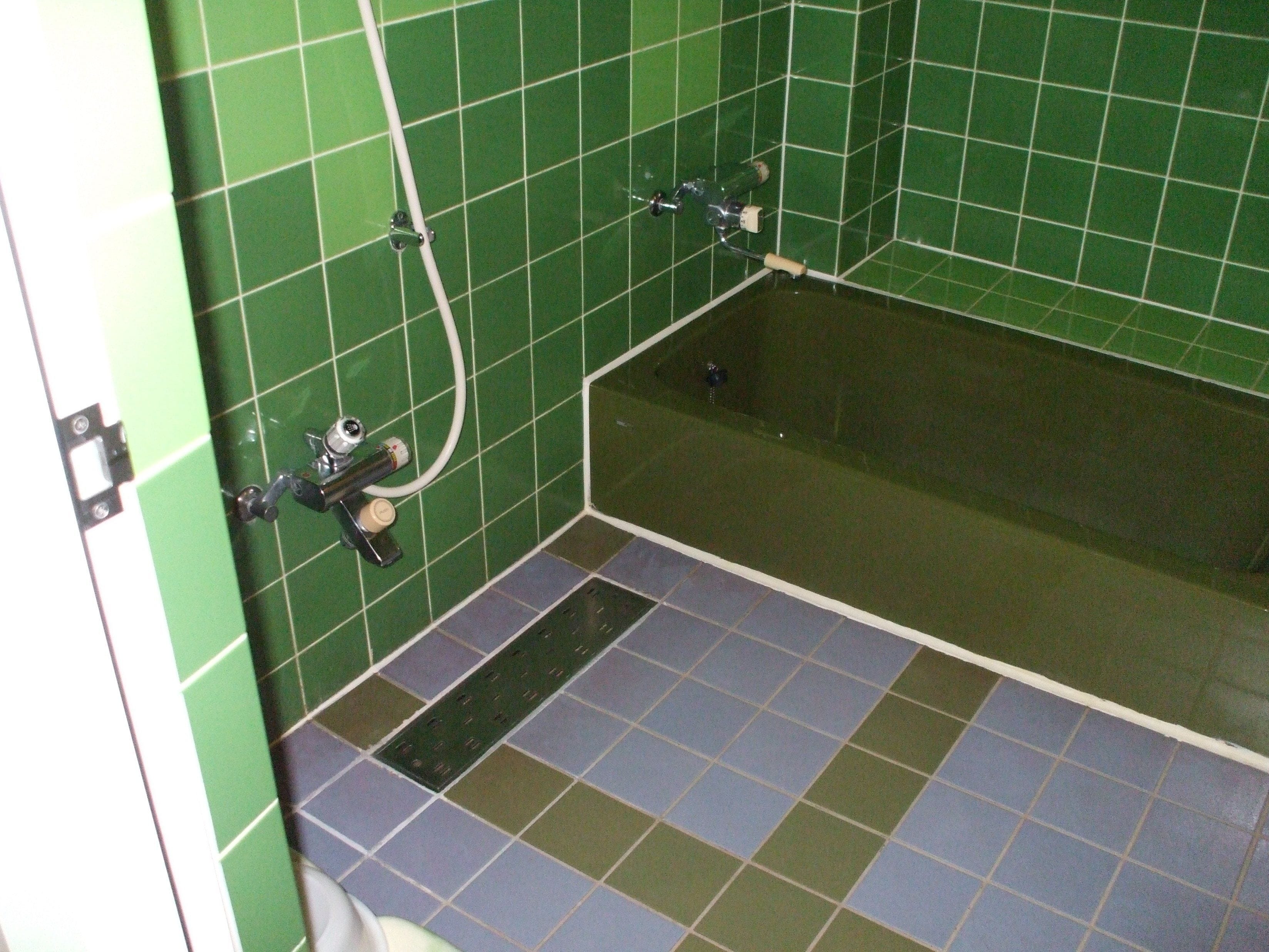 Um banheiro com paredes revestidas de azulejos verdes e piso de azulejos azul e verde.