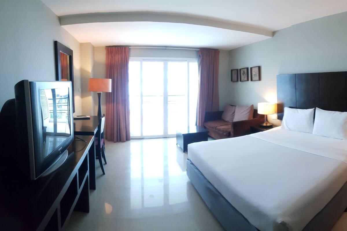 Quarto de hotel com uma cama grande, televisão, escrivaninha e janela com cortinas.