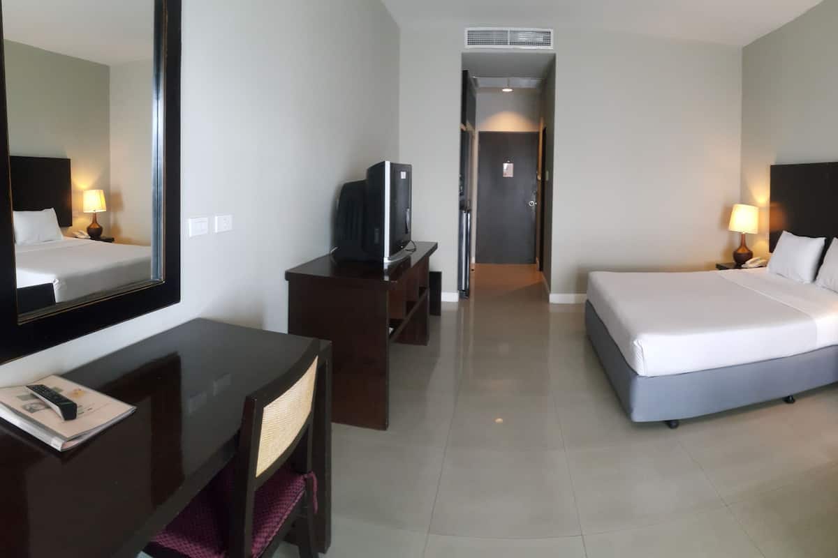 Quarto de hotel com uma cama, escrivaninha, televisão, sofá e espelho.
