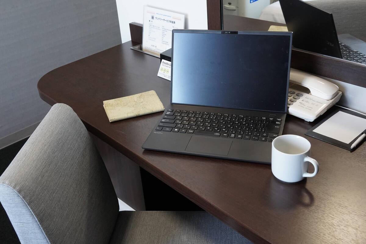 Um laptop sobre uma mesa com uma caneca branca, um bloco de notas e um telefone.