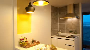 Uma cozinha moderna com bancada branca, duas luminárias pendentes, fogão embutido e janela com vista.