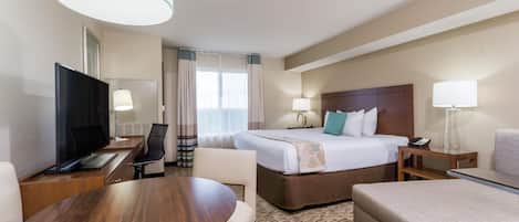 Quarto de hotel com uma cama, uma escrivaninha com televisão, uma cadeira, uma mesa e um abajur.
