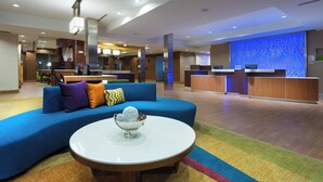 Um hall de hotel moderno com um sofá azul, uma mesa redonda com uma tigela decorativa e um balcão de recepção com iluminação azul.