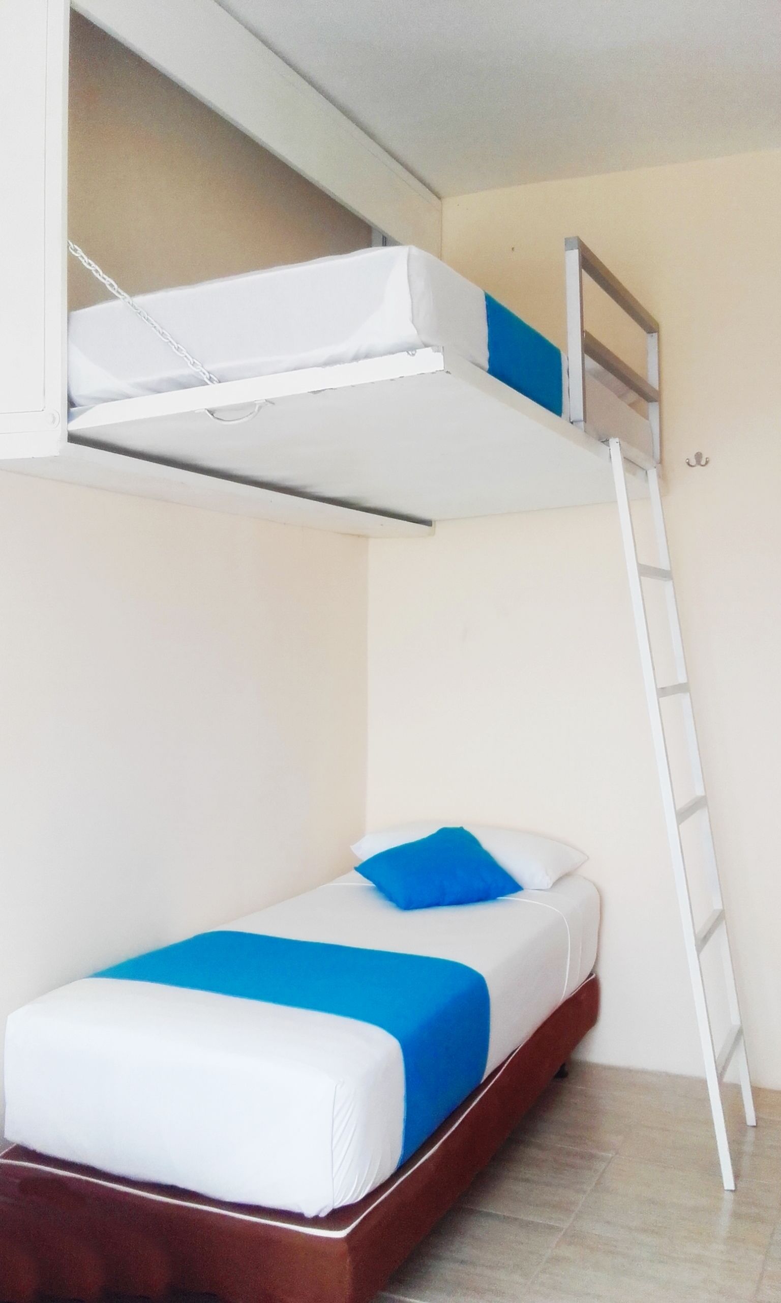 Uma cama beliche com escada, uma cama de solteiro embaixo e um travesseiro azul.