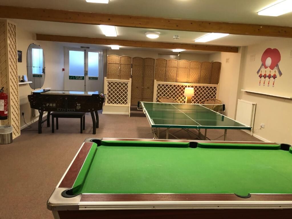Uma sala de bilhar com mesa de sinuca, mesa de snooker e mesa de pingue-pongue.