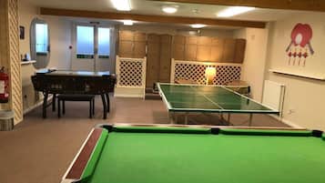 Uma sala de bilhar com mesa de sinuca, mesa de snooker e mesa de pingue-pongue.