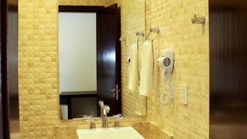 Um banheiro com parede revestida de azulejos bege, pia com espelho, porta-toalhas e secador de cabelo.