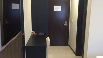 Quarto de hotel com uma cama, escrivaninha, cadeira, televisão e porta.