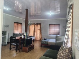 Quarto com cama, escrivaninha, cadeira, televisão e ventoinha.