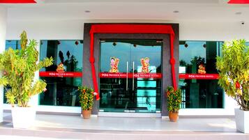 Exterior do Premier Hotel 906, com toldo vermelho, grandes janelas de vidro e vasos de plantas.