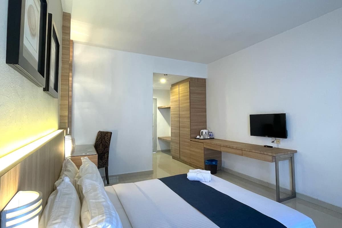 Quarto de hotel com cama, abajur, televisão, escrivaninha e espelho.