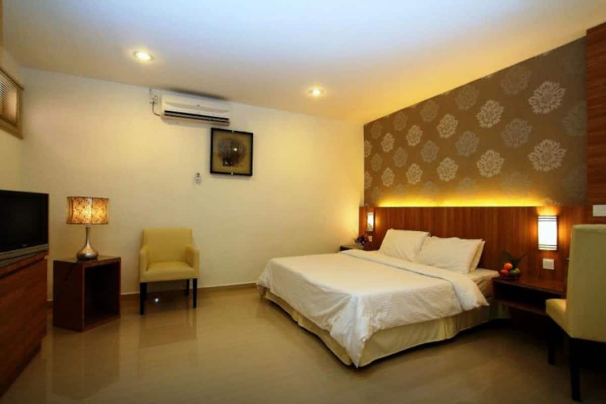Quarto de hotel com cama, televisão, poltrona, abajur e parede com padrão floral.