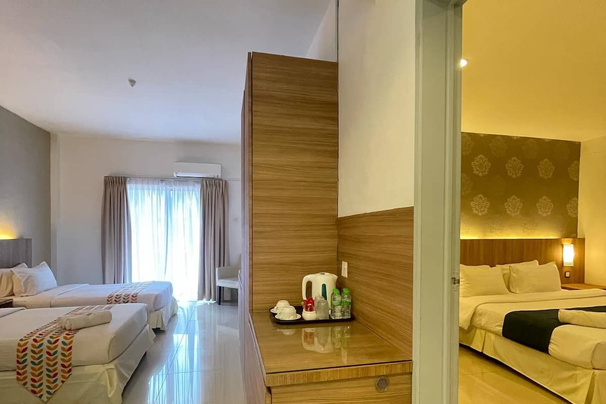 Quarto de hotel com duas camas, divisória de madeira, pequena cozinha e banheiro com chuveiro.