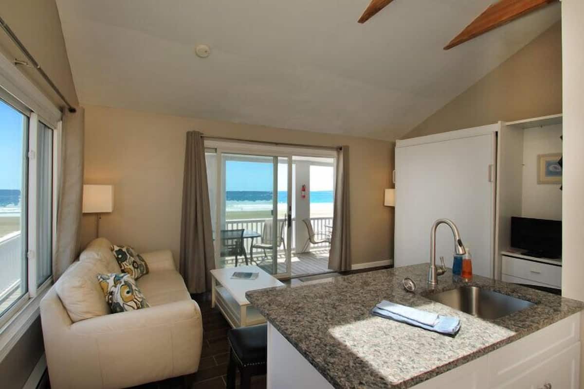 Quarto de hotel com varanda, cozinha compacta, sofá e televisão.