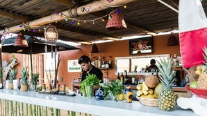 Uma área de bar com balcão, diversas garrafas e frutas tropicais.