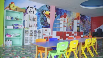 Uma sala de brincadeiras infantil com mobiliário colorido, um recorte de panda e murais educativos.