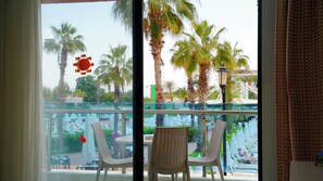 Varanda com duas cadeiras de vime, uma mesa pequena e vista para área da piscina com palmeiras e um poste de luz.
