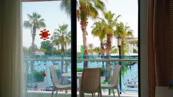 Varanda com duas cadeiras de vime, uma mesa pequena e vista para área da piscina com palmeiras e um poste de luz.