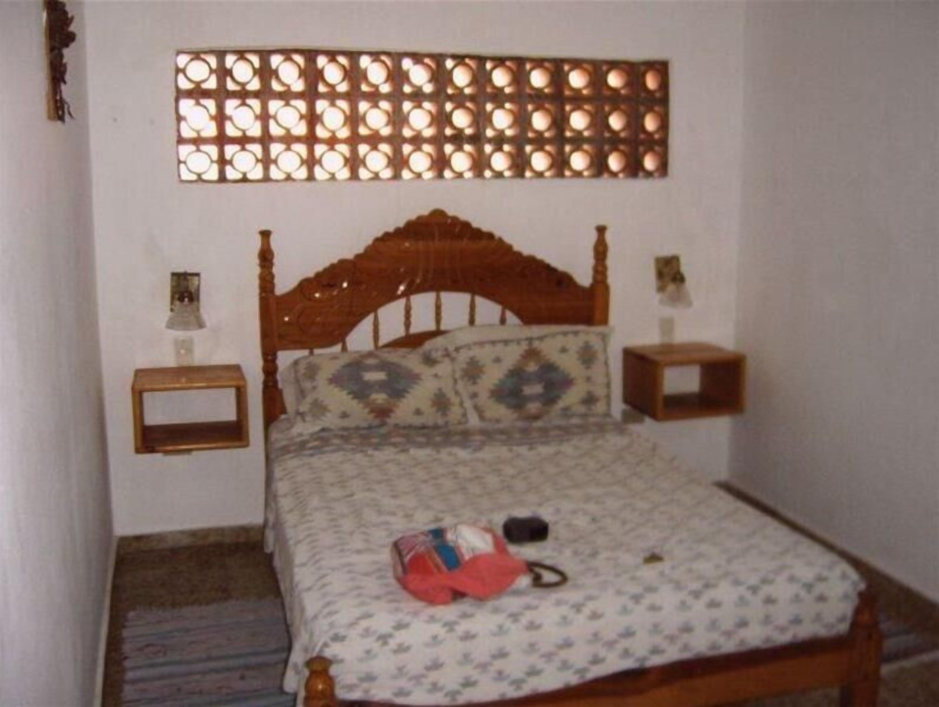 Um quarto simples com uma cama de madeira, um cobreleito estampado e um painel decorativo acima da cama.