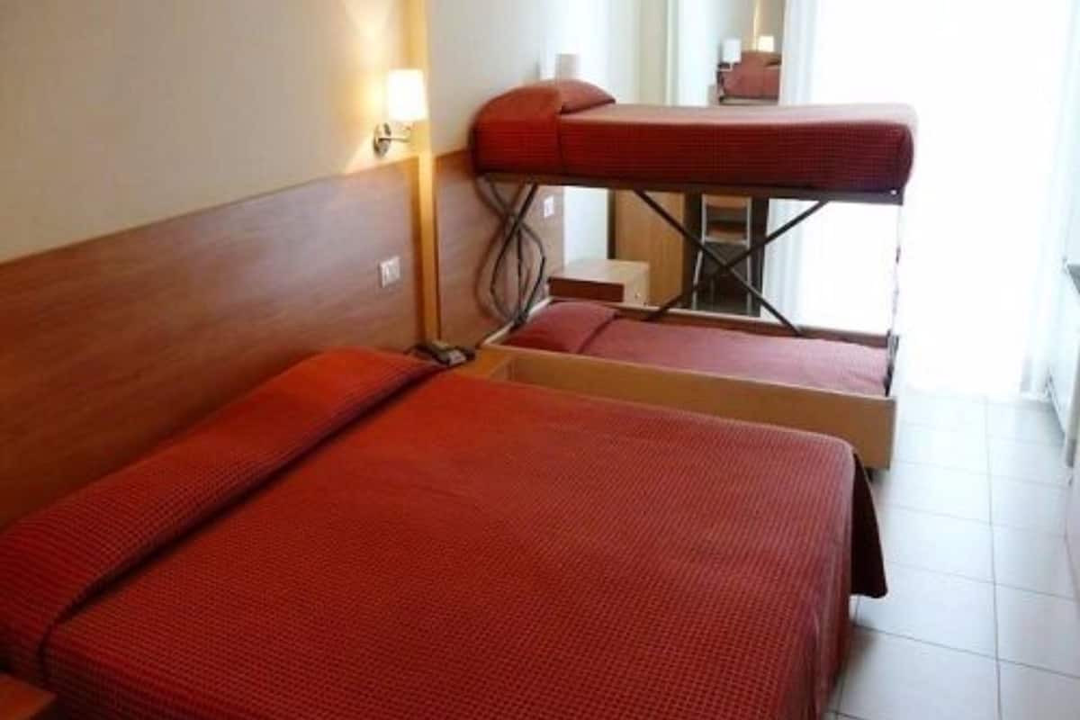Quarto de hotel com duas camas, cada uma com colcha vermelha, e cabeceira de madeira.