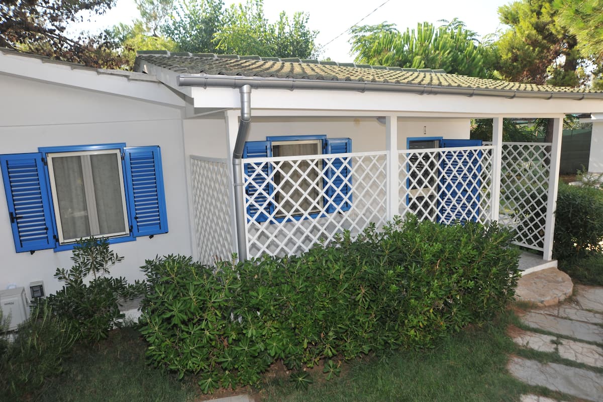 Um edifício branco com persianas azuis, um alpendre coberto e uma cerca branca treliçada.