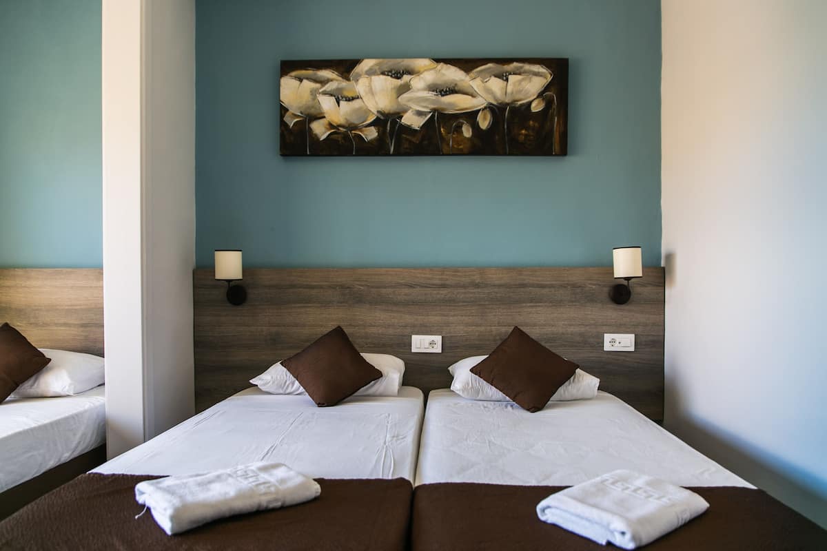 Quarto de hotel com duas camas, cabeceira de madeira, pintura de flores e duas luminárias fixadas na parede.