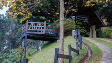 Uma ponte de madeira com um banco, rodeada por árvores e um caminho de pedra.