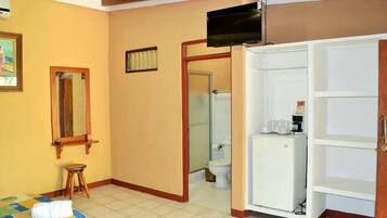 Quarto de hotel com cama, televisão, guarda-roupa e banheiro visível por uma porta aberta.