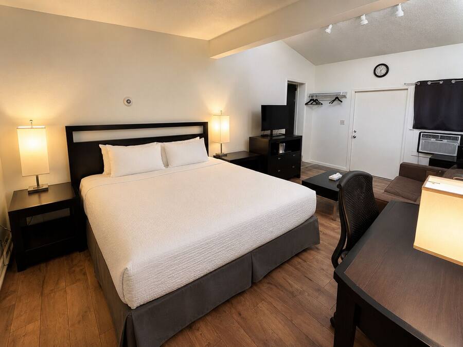 Quarto bem arrumado com cama, mesas de cabeceira, televisão, escrivaninha e uma cadeira.