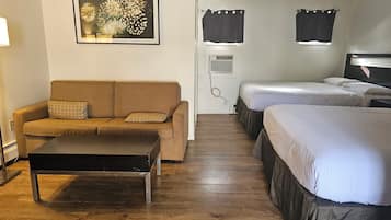 Quarto com sofá, mesa pequena, duas camas, janela com cortinas e ar-condicionado fixado na parede.